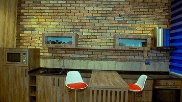Cozinha com painel de parede de tijolos, armários de madeira, micro-ondas, pia e duas cadeiras vermelhas e brancas.