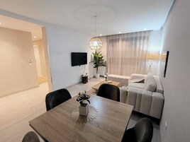 Sala de estar moderna com área de jantar, sofá cinza, TV fixada na parede e planta em vaso.