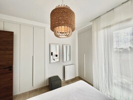 Quarto com uma cama grande, uma luminária pendente de fibra, dois espelhos na parede, um radiador e um guarda-roupa de madeira.