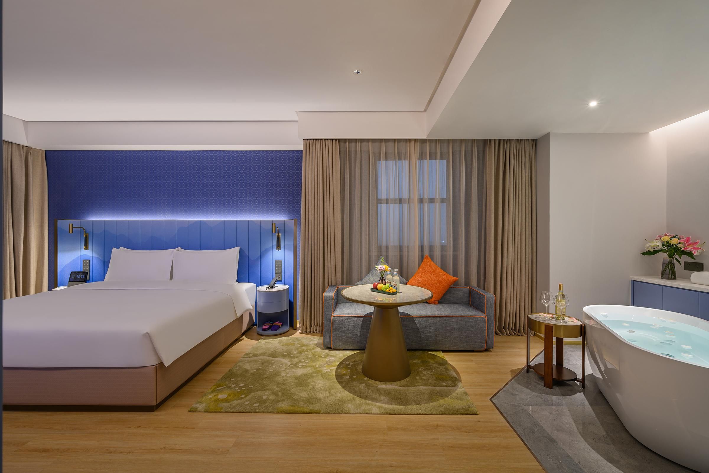 Quarto de hotel moderno com uma cama grande, um sofá, uma mesa redonda, uma banheira e uma pequena mesinha de apoio.