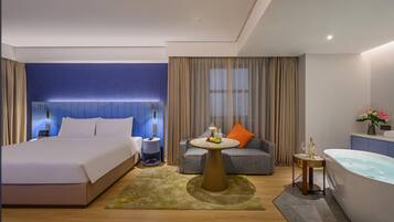 Quarto de hotel moderno com uma cama grande, um sofá, uma mesa redonda, uma banheira e uma pequena mesinha de apoio.