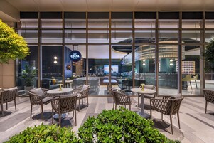 Um hall de hotel moderno com paredes de vidro, móveis de vime e um letreiro da Costa Coffee.