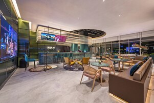 Uma área de convívio moderna com assentos, um bar e um grande ecrã digital.