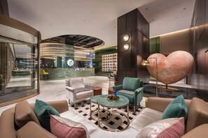 Um lobby moderno com balcão de recepção curvo, área de estar com sofás de couro, piso de mármore e uma grande peça decorativa em formato de coração.