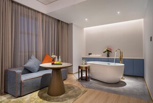 Casa de banho moderna com uma banheira independente, um sofá com almofadas, uma pequena mesa redonda e um vaso decorativo.