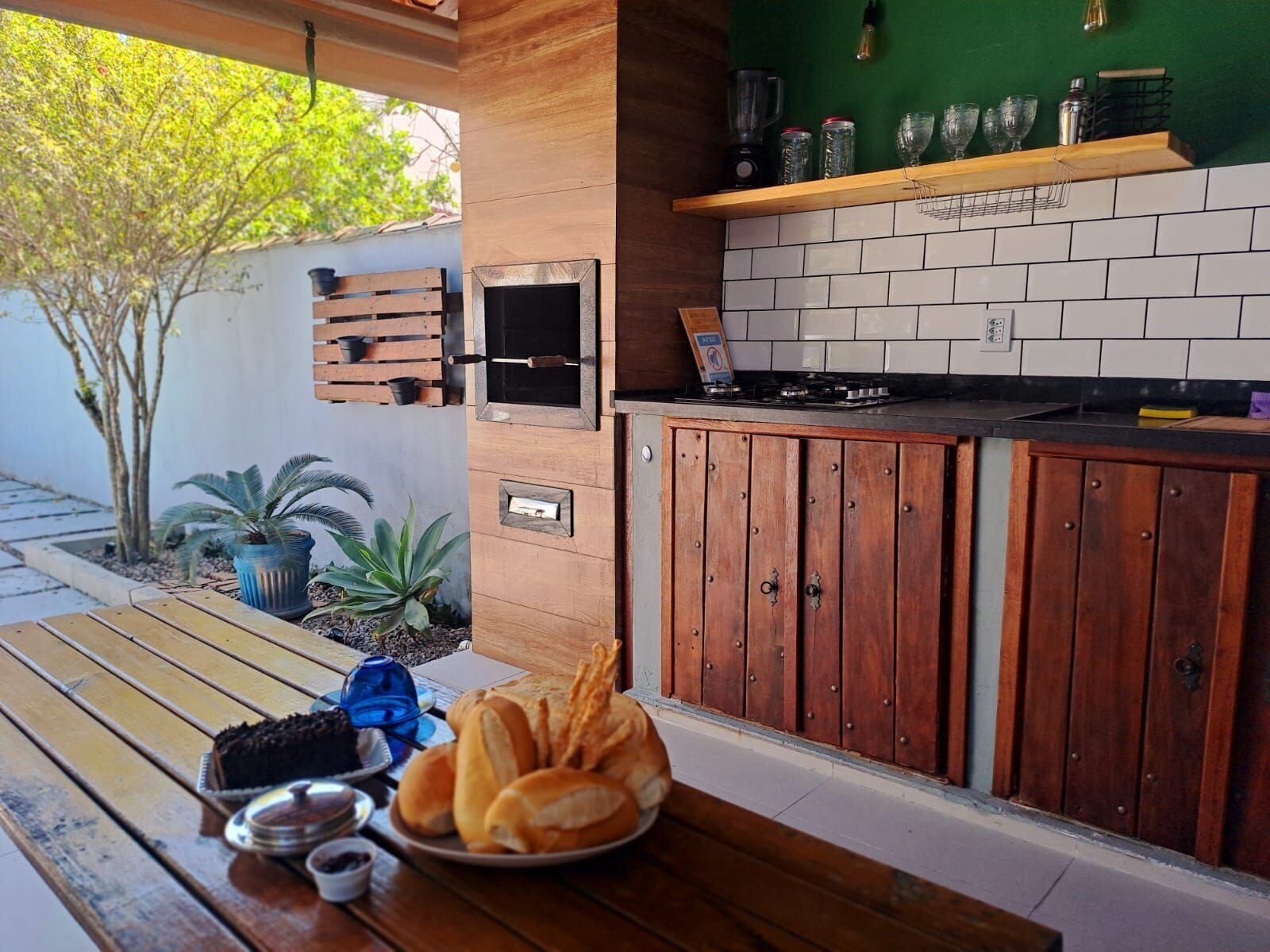 Cozinha com bancada de madeira, forno embutido e parede verde. Lá fora, um banco de madeira com um prato de comida e uma garrafa azul.