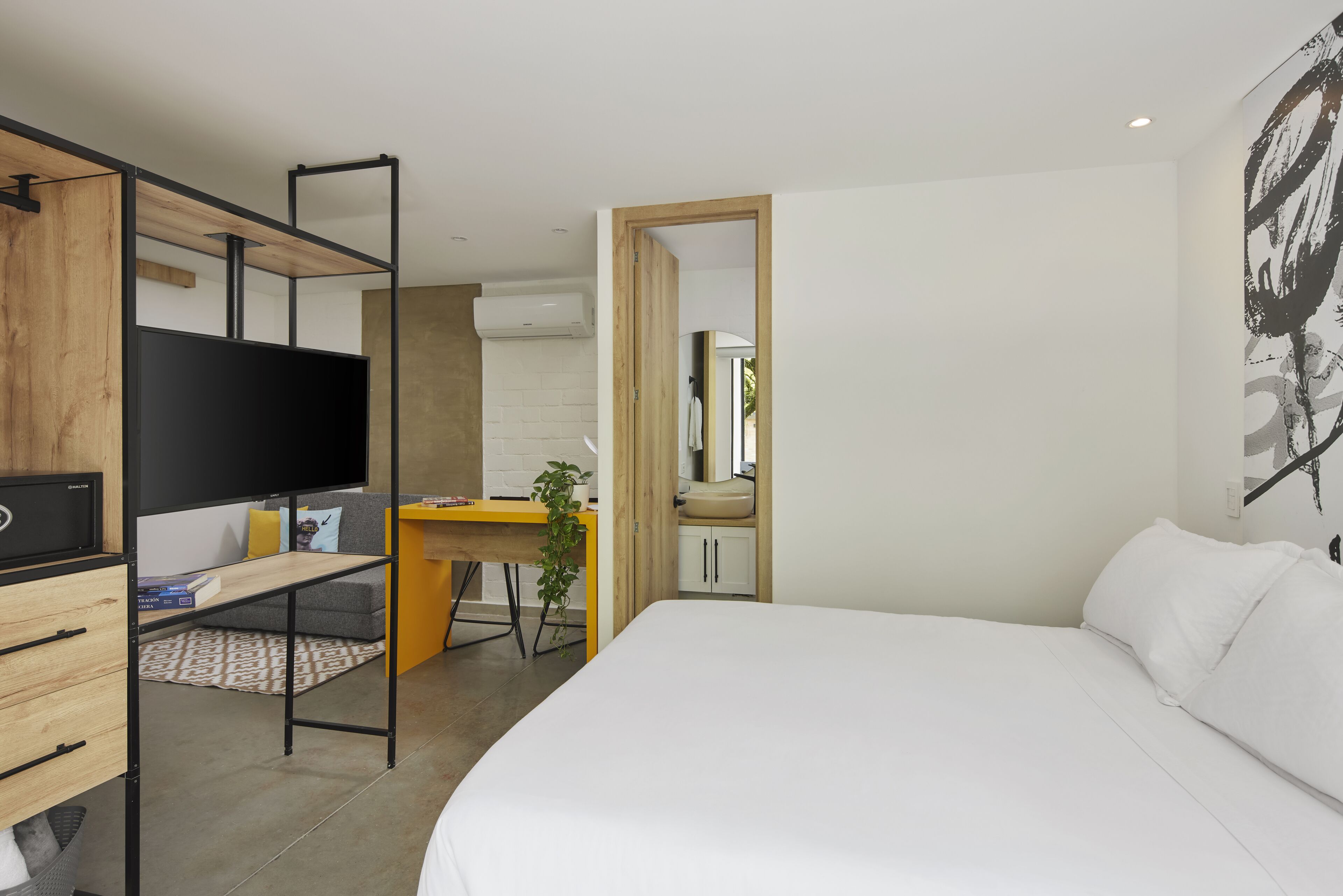 Quarto de hotel moderno com uma cama grande, uma mesa de escritório com computador, TV e guarda-roupa de madeira.