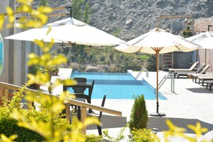 Uma área de piscina com espreguiçadeiras e guarda-sóis, rodeada por vegetação e paisagem rochosa.