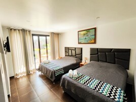 Quarto de hotel com duas camas, um quadro, uma televisão e varanda com cortinas.