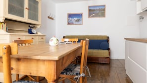Um quarto aconchegante com uma mesa de jantar de madeira, cadeiras, um sofá com almofadas, um armário com espelho e duas quadros emoldurados na parede.