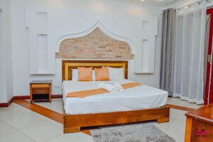 Uma cama bem arrumada com cabeceira de madeira, uma mesinha de cabeceira pequena e um tapete cinza no chão.