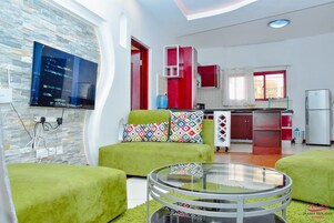Uma sala de estar moderna com um sofá verde, uma mesa de centro de vidro e uma TV de tela plana fixada em uma parede de pedra.