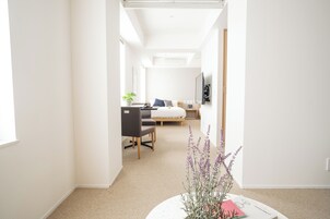 Quarto de hotel moderno com cama, escrivaninha e cadeira, uma mesinha com uma planta, e uma TV fixada na parede.