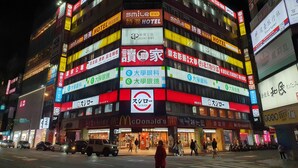 Um edifício de vários andares com diversos estabelecimentos comerciais, incluindo um hotel, um McDonald's e um restaurante taiwanês.