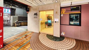 Entrada de um hotel com piso de azulejos, porta de vidro e placa com a inscrição "Just Live Inn".