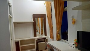 Quarto pequeno com escrivaninha, cadeira, TV e um banquinho.