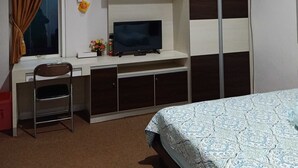 Quarto com cama, escrivaninha com televisão, guarda-roupa e janela com cortinas.
