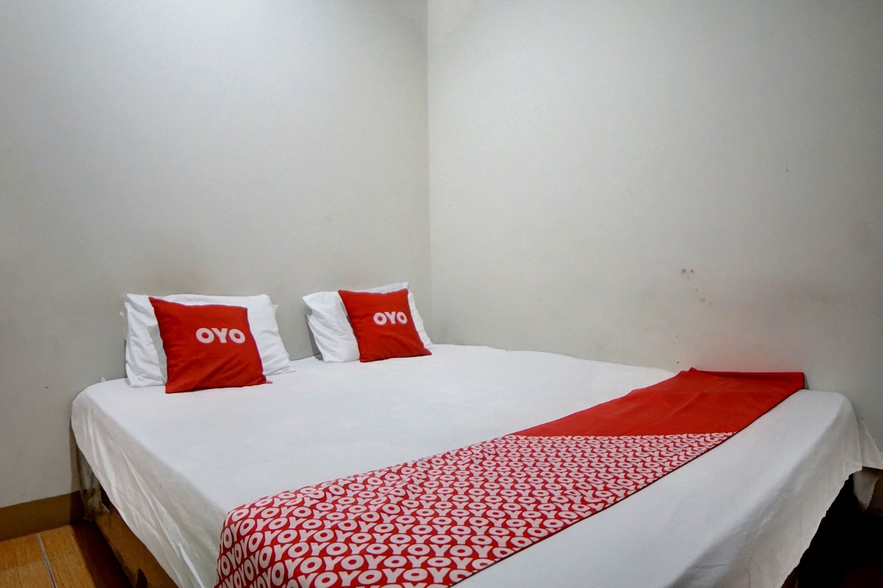 Uma cama de solteiro com roupa de cama branca e detalhes vermelhos, incluindo almofadas e um edredom.
