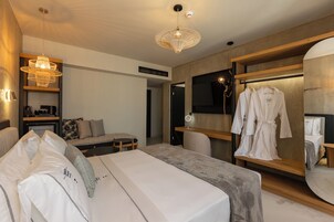 Quarto de hotel moderno com uma cama grande, área de estar, toucador com espelho e suporte para roupões.
