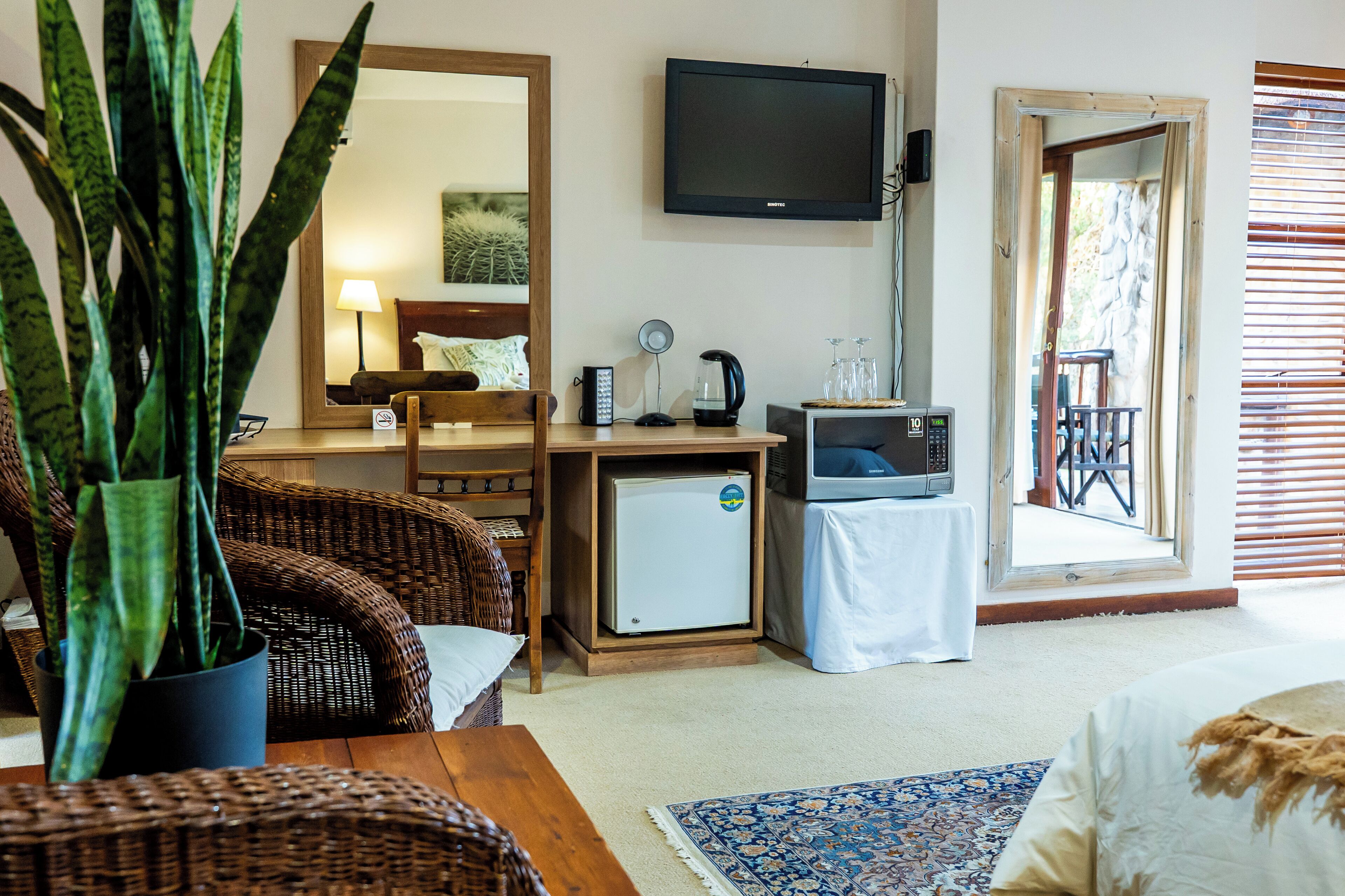 Quarto de hotel com mobiliário de vime, um pequeno frigorífico, televisão e vista para o exterior.