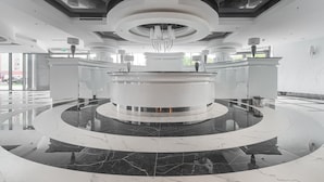 Um hall moderno com uma recepção circular central, pisos de mármore polido e luminárias contemporâneas.