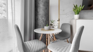 Uma área de jantar moderna com uma mesa redonda, duas cadeiras cinzas estofadas, um vaso de planta e um armário minimalista.