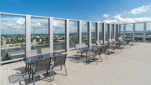 Terraço no telhado com paredes de vidro, área de estar ao ar livre e vista para a cidade.