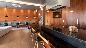 Cozinha moderna com detalhes em madeira, espaço de bar e área de estar com sofá e cadeiras.