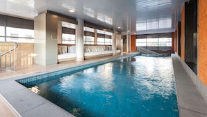 Piscina interna com vista clara, área de estar com sofá e escada que leva a um andar superior.