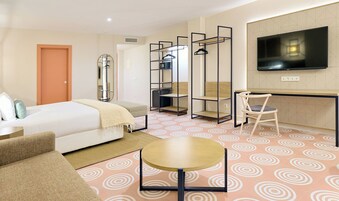 Quarto de hotel com cama, escrivaninha, cadeira, televisão e espelho.