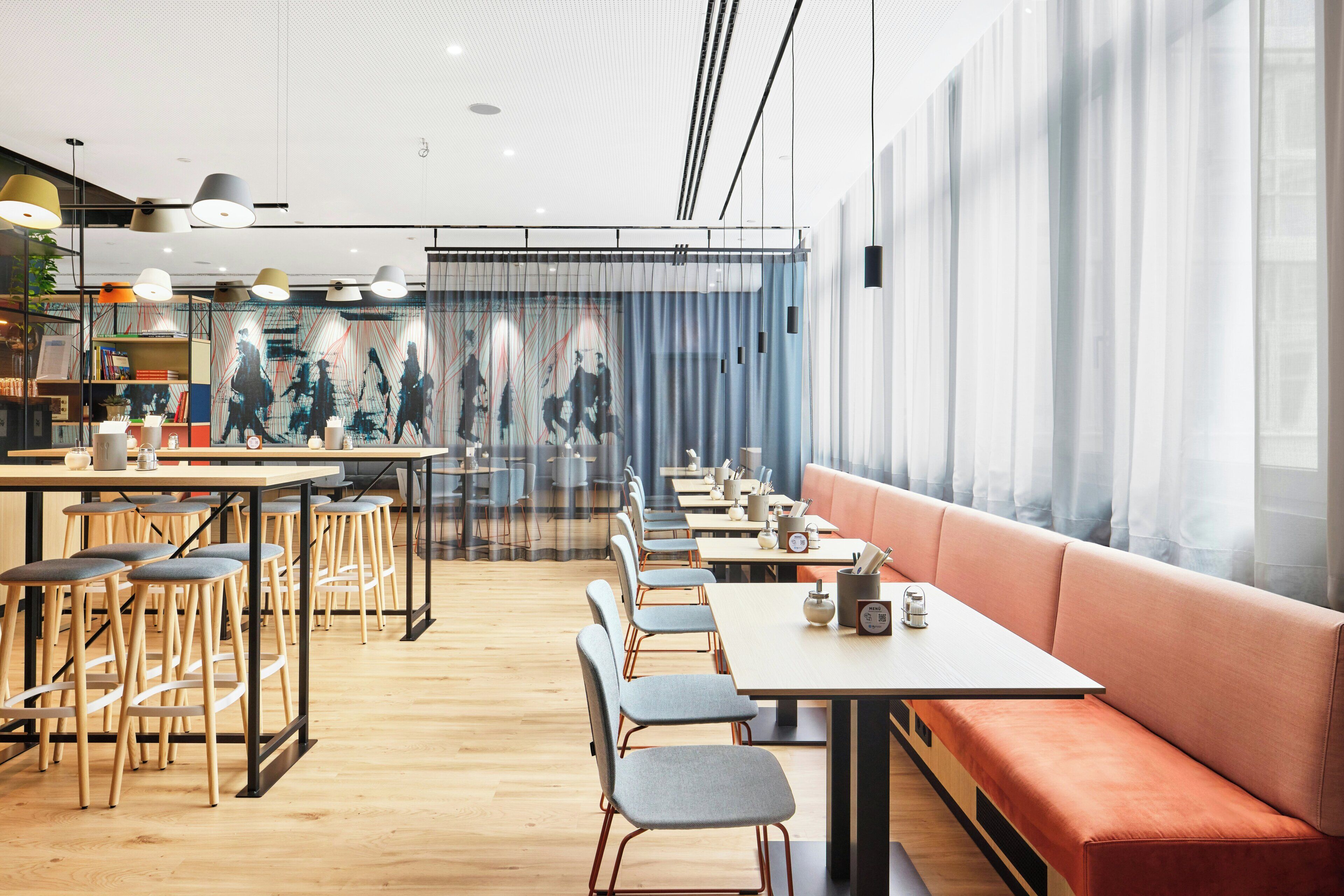 Um café moderno com mesas de madeira, banquetas no balcão e uma área de estar com um banco estofado.