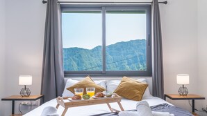 Quarto de hotel com uma cama, bandeja de café da manhã com croissants e suco, e vista para as montanhas pela janela.