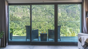 Varanda com duas cadeiras e uma mesa pequena, com vista para uma paisagem verdejante.