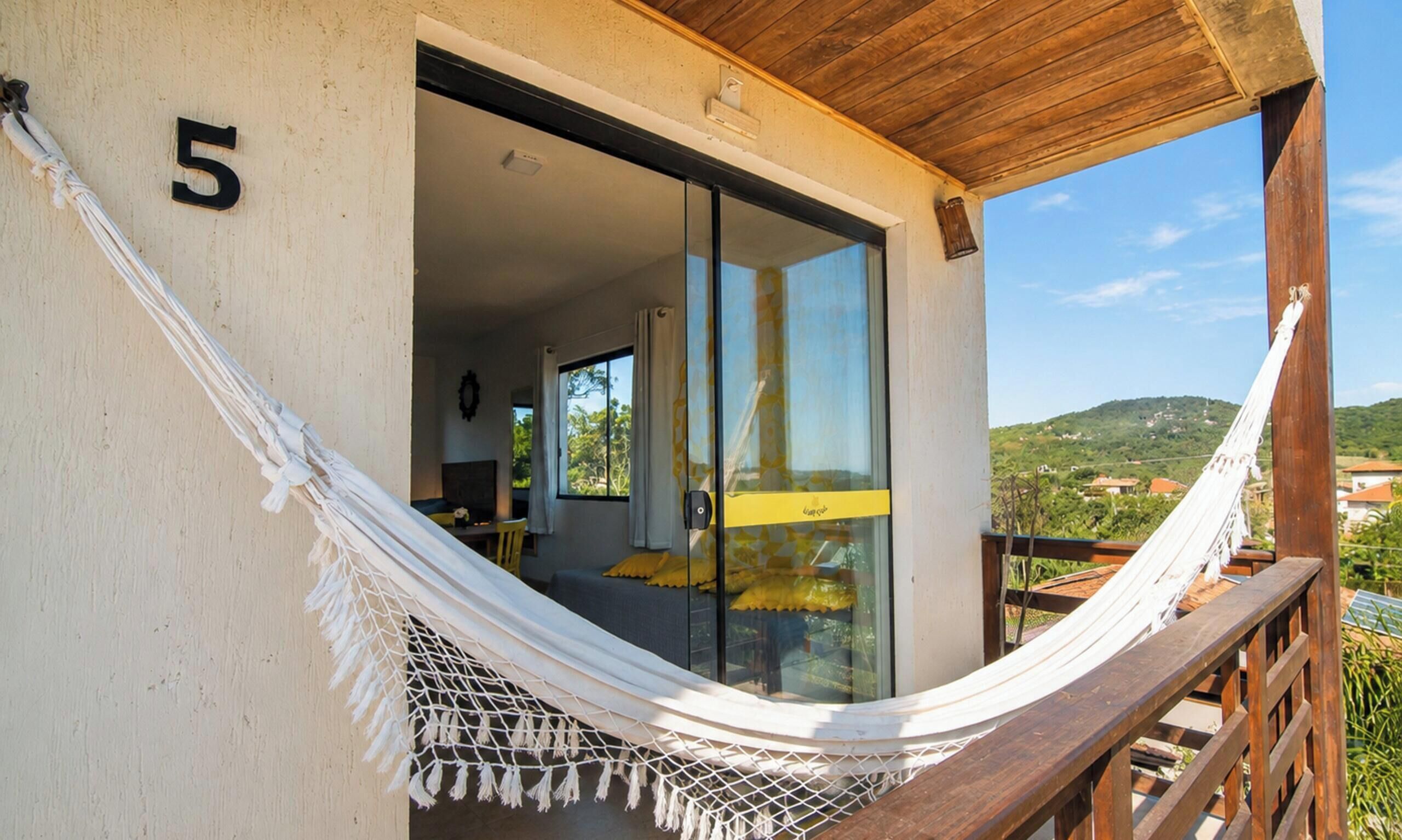 Quarto com rede, porta de correr de vidro e vista para a paisagem.