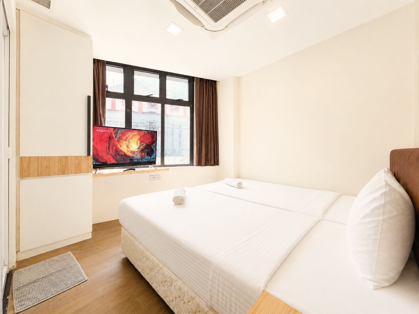 Quarto de hotel com cama, televisão, janela com cortinas e porta.