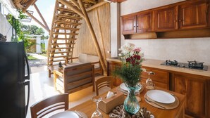 Cozinha moderna com armários de madeira, área de jantar com mesa e cadeiras de madeira, e escada com corrimão de bambu.