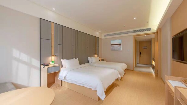 Quarto de hotel com duas camas, uma escrivaninha e uma cadeira. Há um espelho, uma mesa de cabeceira e uma televisão presa à parede.