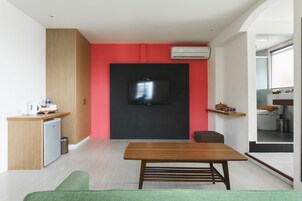 Um espaço compacto com cozinha compacta, televisão de tela plana na parede preta, mesa de madeira e tapete verde.