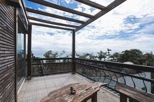 Varanda com vista para o mar, um banco de madeira e guarda-corpo de metal.