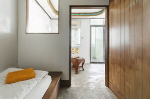 Quarto de hotel com uma cama, um banco de madeira, uma mesa com cadeiras e vista para uma varanda por uma porta aberta.