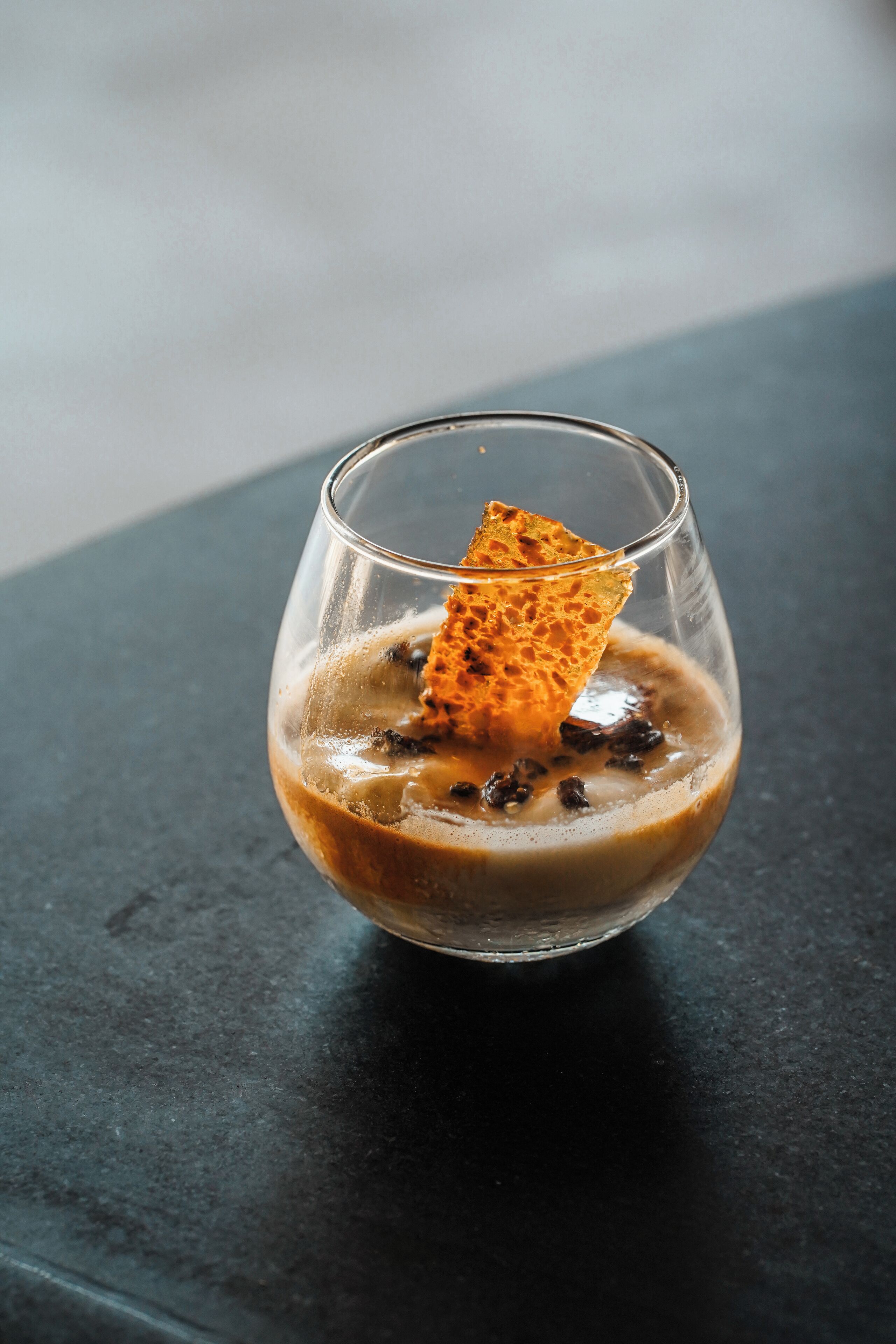 Uma chávena de café com um pedaço de bolo-esponja sobre uma superfície escura.