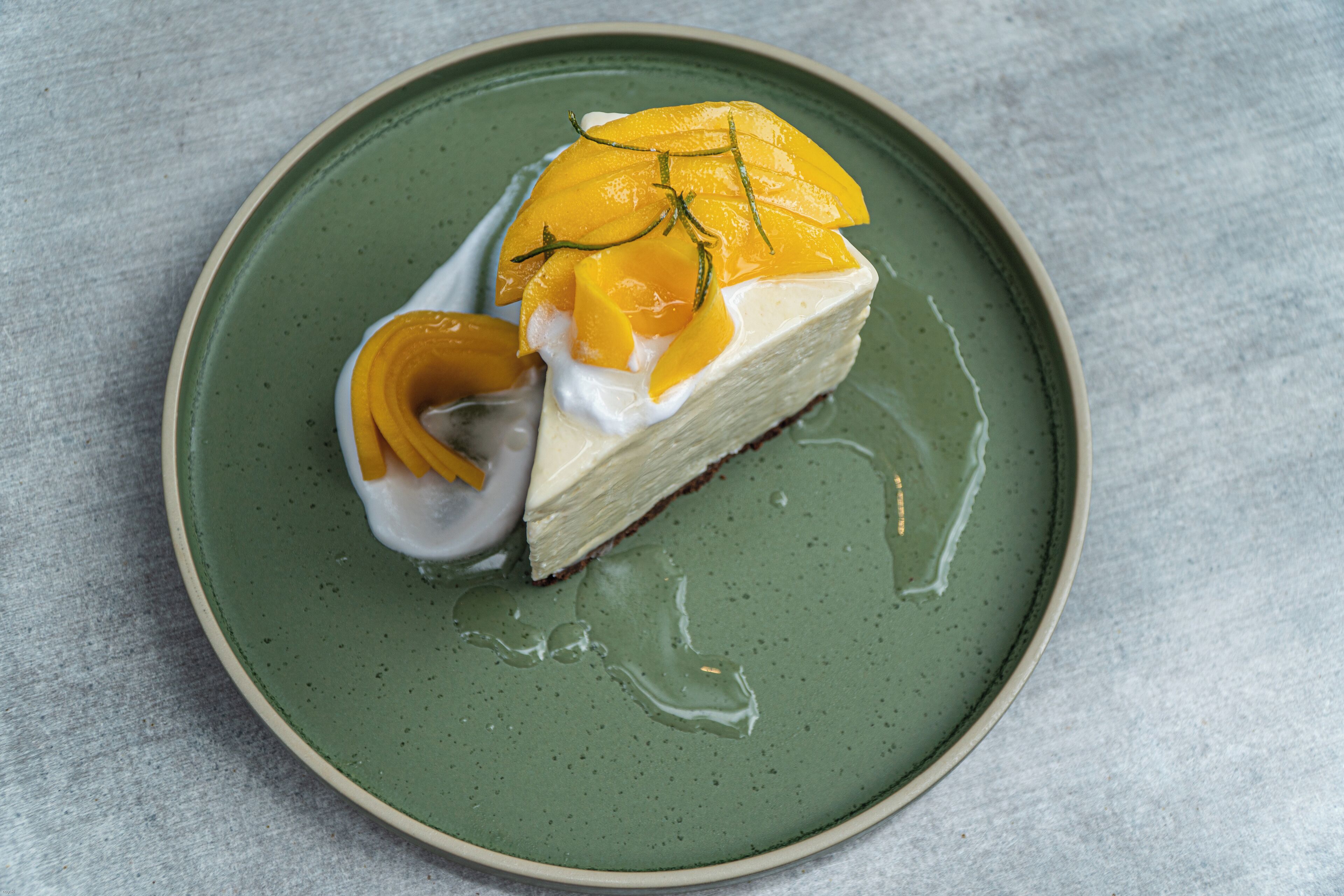 Uma fatia de cheesecake com fatias de manga sobre um prato verde.