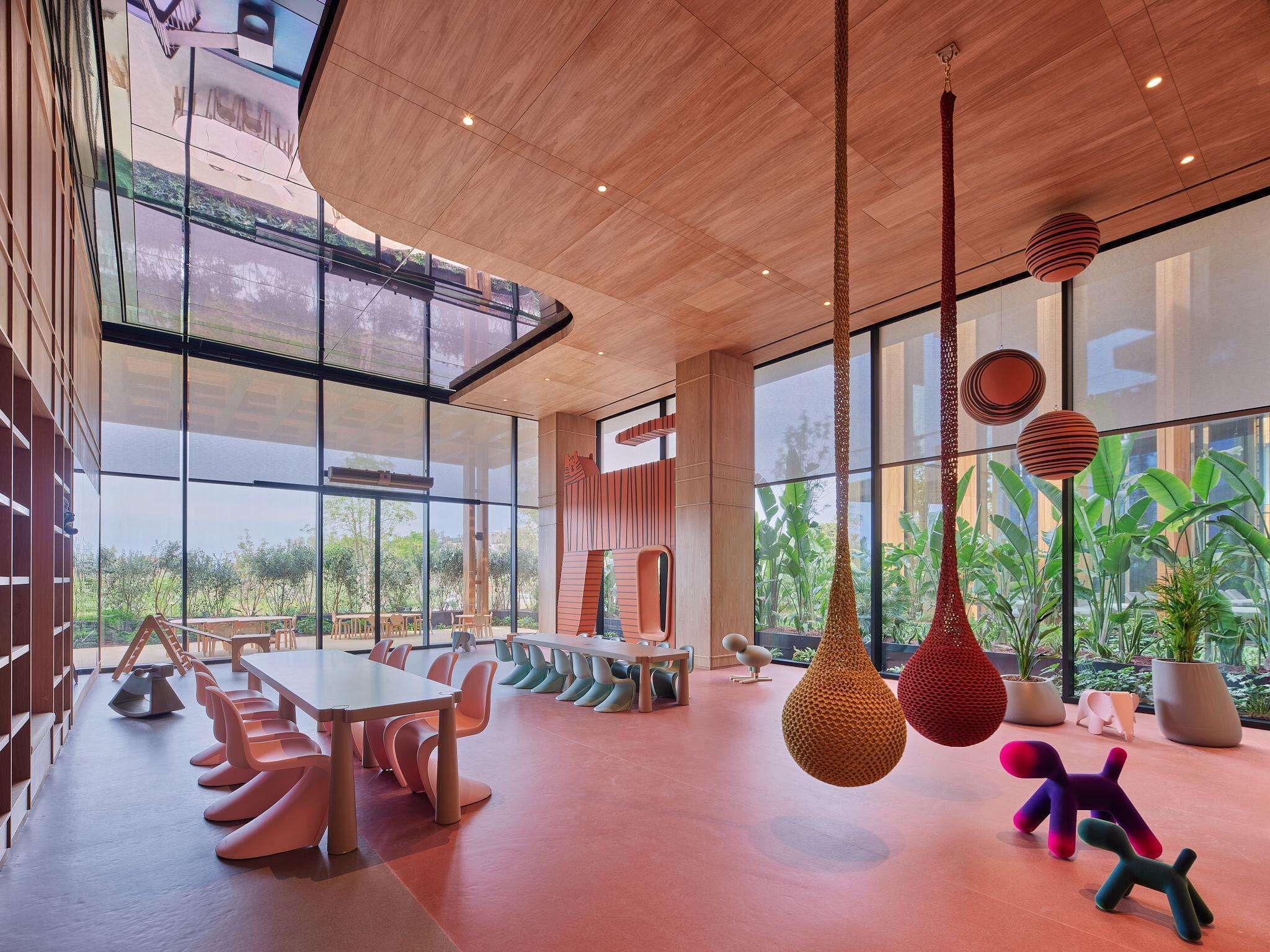 Um espaço amplo e interno com uma mesa comprida e cadeiras, janelas grandes e elementos decorativos pendurados.