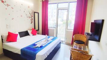 Quarto de hotel com cama, televisão, janela com cortinas e espelho fixado na parede.