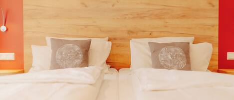 Cama de casal com roupa de cama branca e duas almofadas com desenhos circulares.