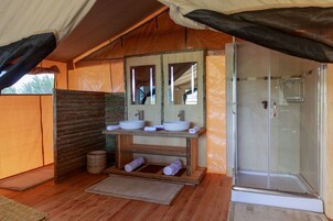 Uma tenda com interior de madeira, incluindo banheiro com duas pias, um espelho e box de vidro.