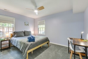 Um quarto com uma cama, uma escrivaninha, uma cadeira, um ventilador de teto e duas janelas.