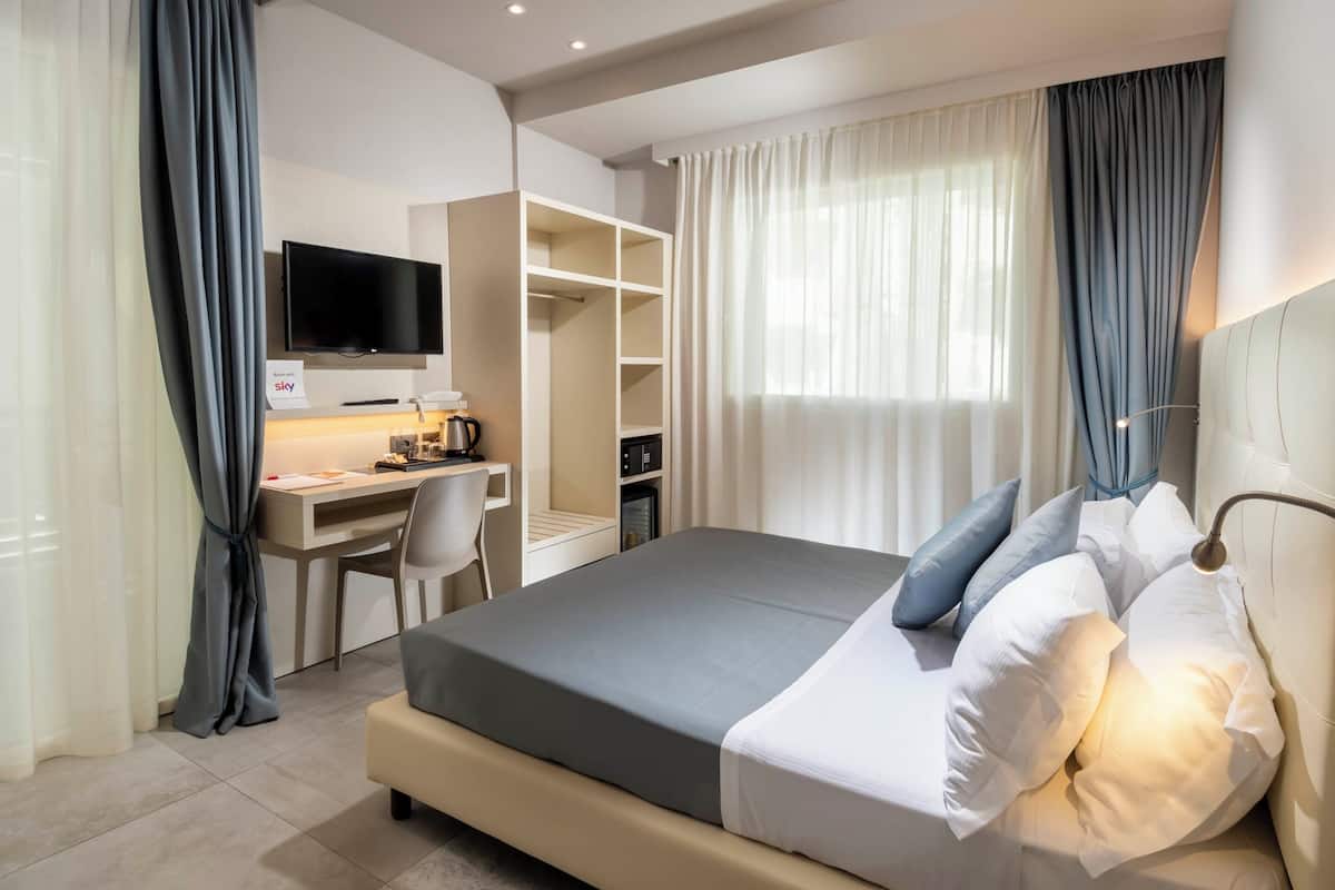 Quarto de hotel moderno com uma cama grande, uma escrivaninha com computador, uma televisão de tela plana e um guarda-roupa.