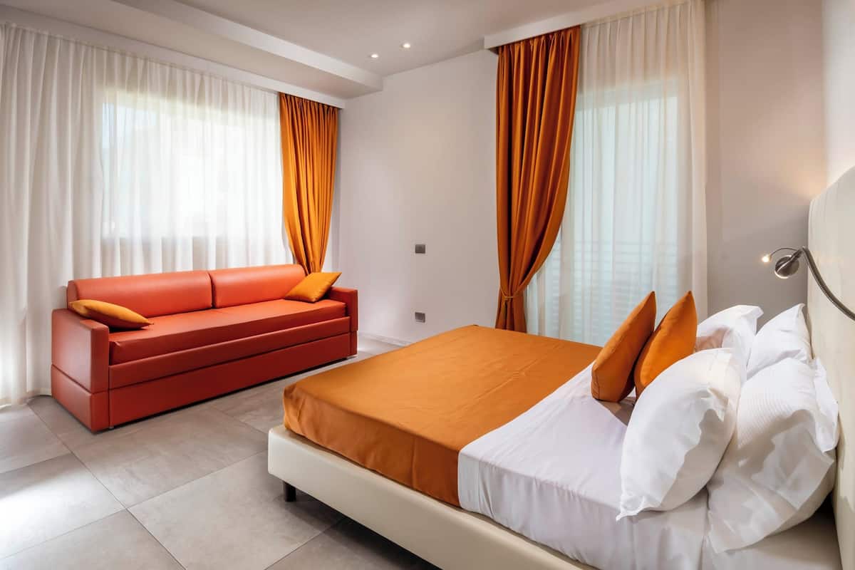 Um quarto moderno com uma cama grande, um sofá vermelho e cortinas laranja.