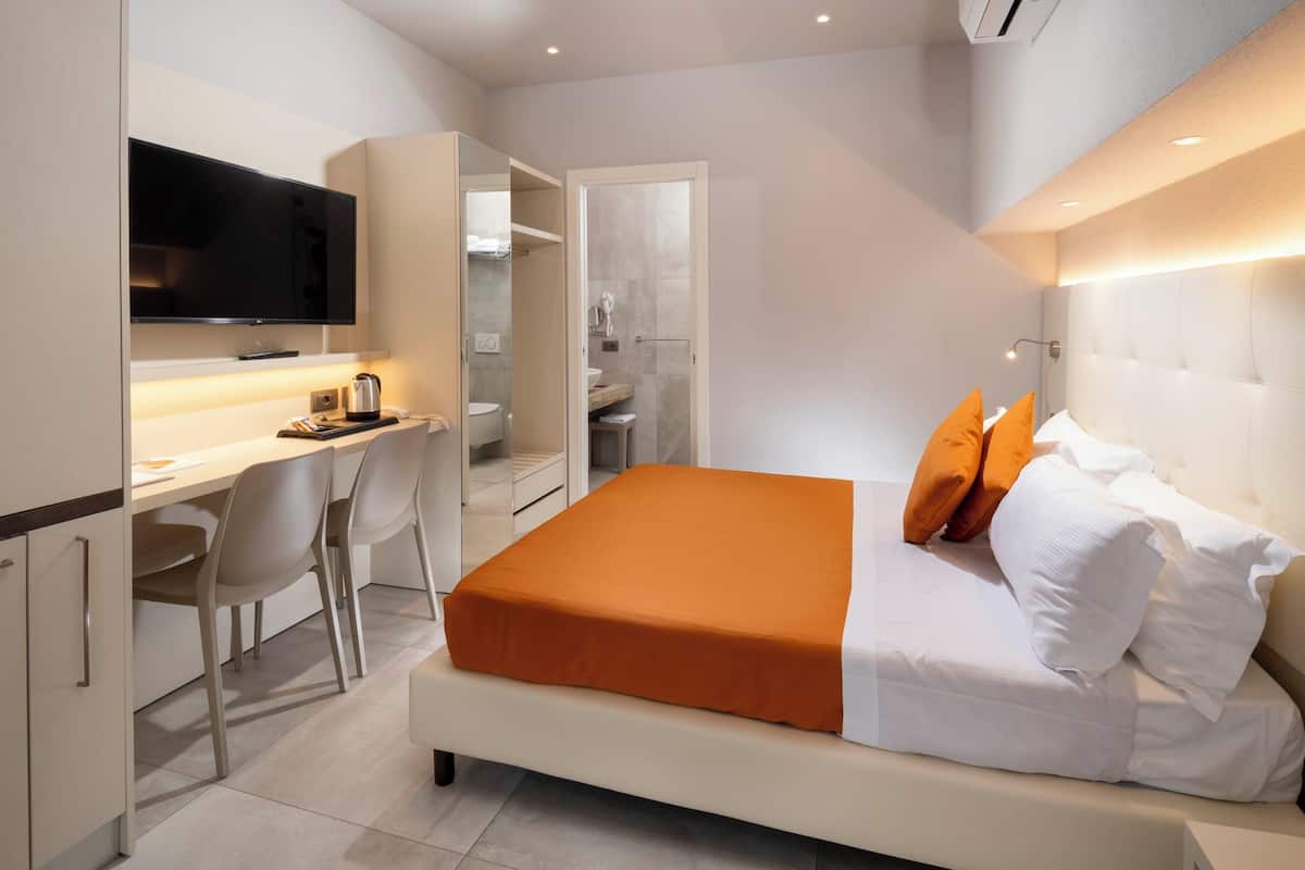 Quarto de hotel moderno com cama, escrivaninha e televisão de tela plana, além de área de chuveiro.